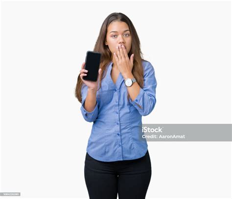 격리 된 배경 표지 입 손으로 이상의 스마트폰 화면을 보여주는 젊은 아름 다운 갈색 머리 비즈니스 여자 실수 두려움 침묵 비밀