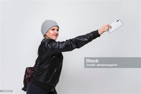 따뜻한 모자와 가죽 재킷을 입은 백인 금발 소녀의 초상화가 하얀 배경에 핸드폰을 던지다수평 구성 20 29세에 대한 스톡 사진 및 기타 이미지 Istock