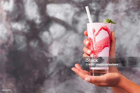 회색 콘크리트 시멘트 질감 벽의 배경에 여성의 손에 빨간 딸기 시럽 신선한 차가운 프라푸치노 의 유리 트렌디 한 힙스터 카페