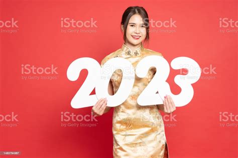 赤い背景に2023年の数字を持つ金色の伝統的なチャイナドレスを着たアジアの若い女性旧正月のコンセプト 1人のストックフォトや画像を多数ご