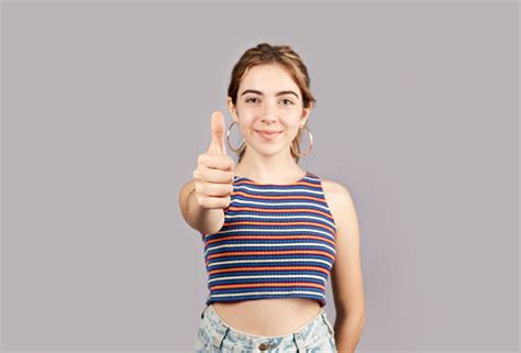 회색 배경에 고립 된 엄지 손가락으로 카메라를보고 포즈를 취하는 젊은 라티나 십대 소녀 공간을 복사합니다 청소년기에 대한 스톡