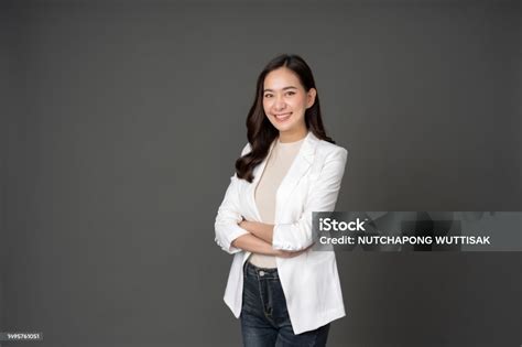 긴 머리를 한 아시아 여성 임원 그녀는 밝게 웃으며 자신 있게 팔짱을 끼고 섰다 그녀는 흰 양복을 입고 있었다 스튜디오에서 회색