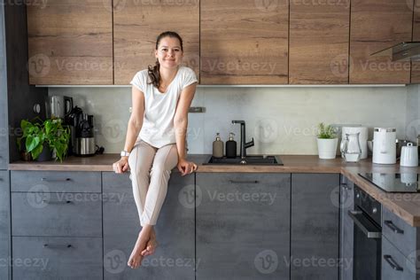 Young Woman Sitting On Her Kitchen Counter At Home High Quality Photo