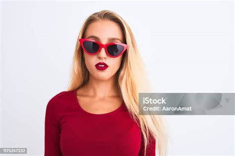 赤いtシャツとサングラスをかけた若い美しい女性は顔に真剣な表情を浮かべて孤立した白い背景の上にシンプルで自然なカメラを見て 1人のストック