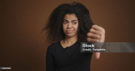 성가신 아프리카 계 미국인 소녀 보여주는 엄지 손가락 아래로 기호 에 싫어하는 에 갈색 벽 갈색에 대한 스톡 사진 및 기타
