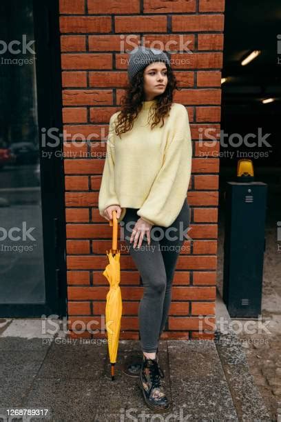 노란 스웨터와 회색 모자를 입은 매력적인 젊은 곱슬 거리는 소녀가 우산을 들고 벽돌 벽에 머무는 동안 다리 신체 부분에 대한 스톡 사진 및 기타 이미지 Istock