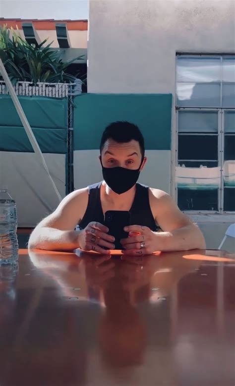 A Man Wearing A Mask Sitting At A Table With His Cell Phone In Front Of Him