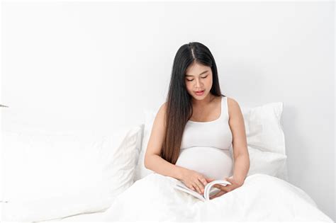 아시아 행복 임산부는 앉아서 침대에 책을 읽고 그녀의 배를 만지고있다 임신 모성 사람 및 기대 개념 아시아인에 대한 스톡 사진
