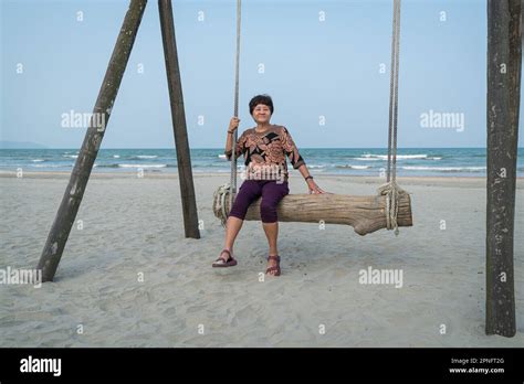 Senior Asian Woman Relaxing On A Wood Plank Swing On The Beach