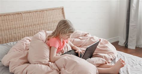 침대에 앉아 가상 온라인 학교 수업에서 배우는 소녀 집에서 노트북 인터넷으로 작업하는 아이 타이핑 무선 기술을 사용하는