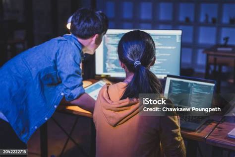 두 명의 젊은 남녀 프로그래머가 밤늦게 따뜻하고 시원한 조명이 있는 사무실에서 함께 코딩 작업을 하고 있습니다 어두운 색에 대한