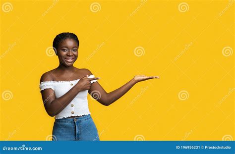 Happy Young African Woman Pointing Finger At Open Palm Over Yellow