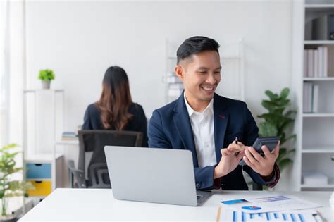 자신감 넘치는 아시아 사업가가 사무실 책상 위에서 노트북과 서류를 들고 일한다 25 29세에 대한 스톡 사진 및 기타 이미지