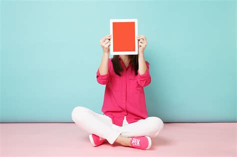 장미 셔츠 블라우스에 전체 길이 세로 여자 바닥에 앉아 흰 바지 잡고 밝은 핑크 블루 파스텔 벽 배경 스튜디오에 고립 된 태블릿