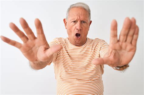 고립 된 흰색 배경 위에 서있는 줄무늬 티셔츠를 입은 선임 회색 머리의 남자가 손바닥 화가 나고 좌절하는 표정으로 중지 제스처를하고 있습니다 T 셔츠에 대한 스톡 사진 및