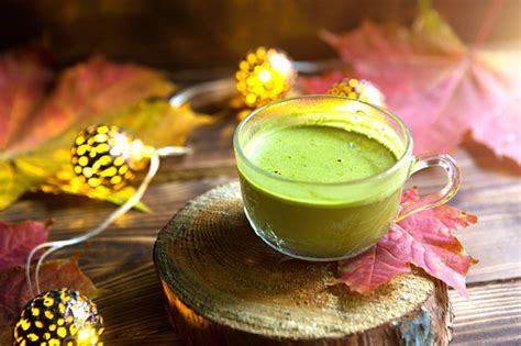 가을 정물에서 나무 테이블에 투명 한 컵에 거품이 있는 녹색 일본 말차 차 따뜻한 분위기와 편안함 조명 화환 붉은 단풍 나무 잎 계피 스틱 호박 쿠키 슬라이스 마시기에 대한