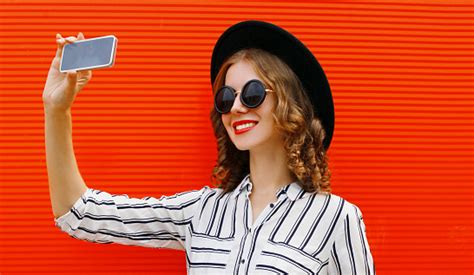 흰색 줄무늬 셔츠 빨간 배경 위에 검은 둥근 모자를 입고 전화로 셀카 사진을 찍는 행복한 미소 여자의 초상화 20 29세에 대한 스톡 사진 및 기타 이미지 Istock