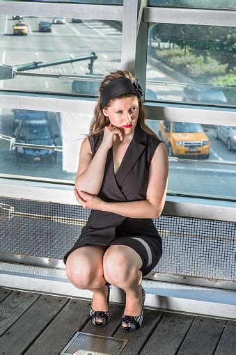 Young Woman Squatting By Glass Wall In New York City Thinking Stock