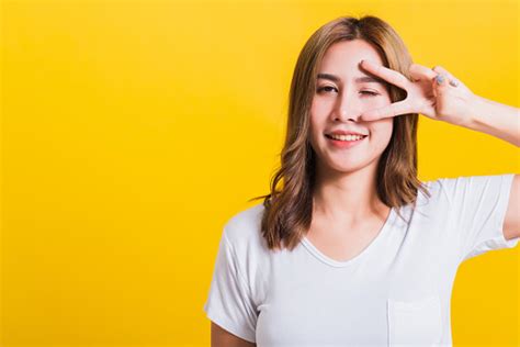 아시아 태국 행복 초상화 아름다운 귀여운 젊은 여자 미소 서 서 서 착용 티셔츠 보여주는 손가락 만들기 V기호 눈 근처 카메라
