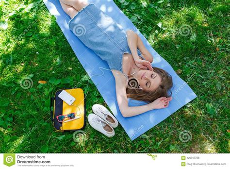 Pretty Young Woman Relaxing On The Grass In A Park Listening To Music