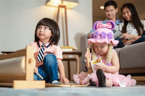 동생은 집 거실의 양탄자에 여동생과 함께 종이를 그려 부모는 멀리 보고 소파에 앉아 배경 가정 개념의 가족 2 3 살에 대한