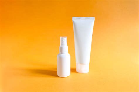 질감이 밝은 오렌지 색 배경에 브랜딩 과 라벨을 위한 두 개의 브랜드가 없는 흰색 병의 모형 그 중 하나는 병 플라스틱 튜브를 짜내는 것입니다 다른 하나는 플라스틱 스프레이