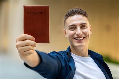 Premium Photo A Joyful Young Man Holding Up A Passport With A Brown