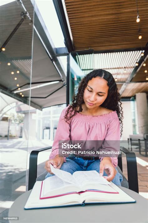 Young Smiling Latin American Student Woman Sitting And Reading A Book