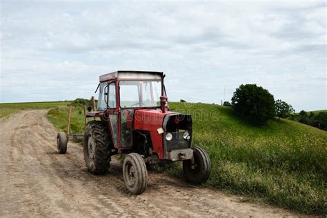 Red Tractor Parked On A Dirt Road In A Hilly Countryside Landscape