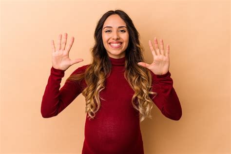 Joven mujer embarazada mexicana aislada sobre fondo beige mostrando el número diez con las manos