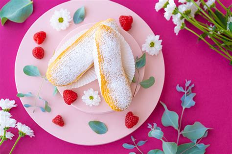 에클레어 케이크 Eclair 커스터드 케이크는 푹시아 배경의 분홍색 연단에 크림과 라스베리가 들어간 케이크입니다 쵸크 패스트리 여름 디저트 위에서보기 0명에 대한 스톡 사진