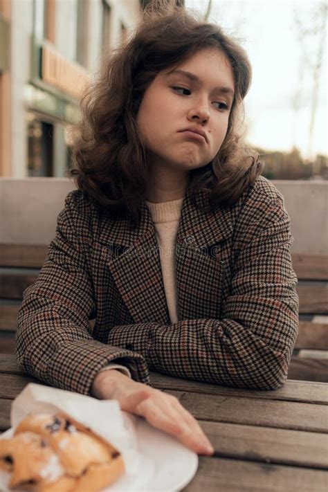A Frustrated Young Girl Eating Sweet Tasty Cupcake In Outdoor Cafe