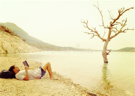 Maschio Che Si Rilassa Da Un Lago Che Legge I Piedi Nudi Di Un Libro
