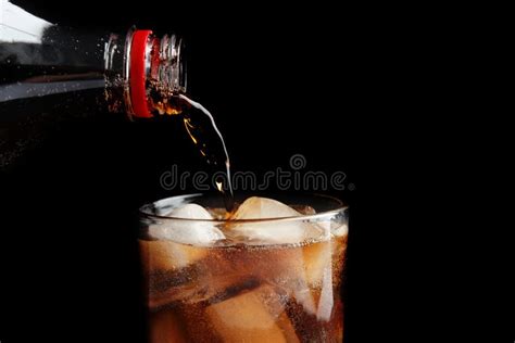 Pouring Refreshing Cola From Bottle Into Glass With Ice Cubes On Black