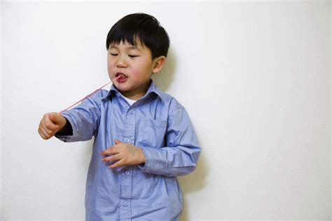 东方人儿童一个人站举闭眼横图室内白天白色背景正面纯洁亚洲仅一个男性仅一个人咬服装棒棒糖食品糖糖果甜点