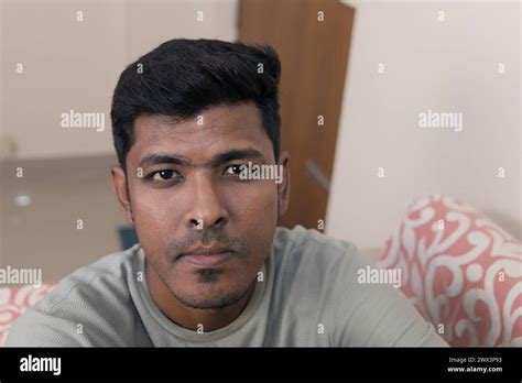 A Thoughtful Indian Man Sits On A Couch Gazing Directly At The Viewer
