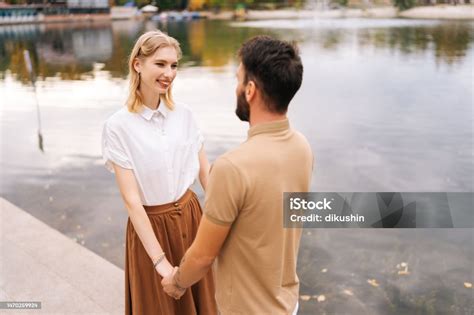 알아볼 수 없는 수염 난 남자가 도시 공원의 아름다운 호수 옆에 야외에 서서 서로를 바라보고 있는 매력적인 금발 여자와 이야기하는 뒷모습 일체감에 대한 스톡 사진 및 기타