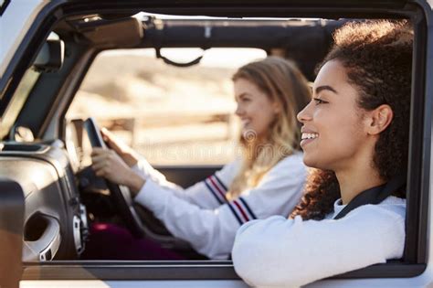 Two Young Female Friends Driving A Car In The Sun Side View Stock