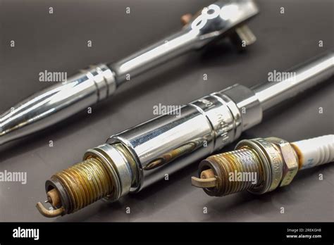 A Socket Wrench An Extension Bar With A Spark Plug Socket Attached And Two Used Spark Plugs