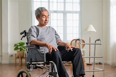 집에서 휠체어에 앉아 창문 밖을 내다보는 노인의 샷 휠체어를 타고 혼자 집에 머물러있는 노인 남성이 거실에서 창문 밖을 바라