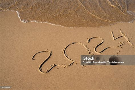 새해 개념입니다 텍스트 2024 모래 표면에 손으로 쓴 글씨 푸른 바다의 파도가 해변에서 숫자를 씻어냅니다 2024년 새해 복