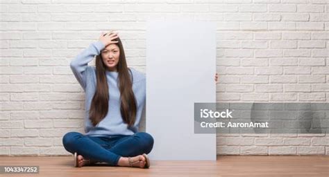 머리에 손으로 압박 하는 배너를 들고 벽돌 벽을 통해 젊은 중국 여자는 수치심과 깜짝 얼굴로 충격 분노와 좌절 두려워 하 고