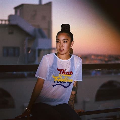 A Woman Sitting On Top Of A Balcony Next To A Tall Building At Sunset With The Sun Setting