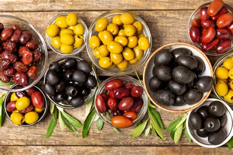 ชุดของมะกอกสีเขียวสีแดงและสีดําบนพื้นหลัง มะกอกชนิดต่าง ๆ ในชามและน้ํามันมะกอกที่มีใบมะ ภาพสต็อก