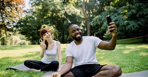 공원에서 요가 재미있는 젊은 다민족 가족 커플이 Youga를 준비하고 야외에서 운동하고 맞는 매트에 앉아 스마트폰으로 사진을 찍는 수평 사진 건강한 라이프 스타일의
