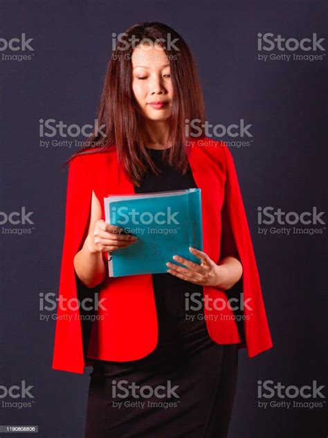 우아한 빨간 양복을 입은 중년 아시아 비즈니스 레이디는 손에 파란색 폴더가있는 어두운 배경에 서 있습니다 Classical