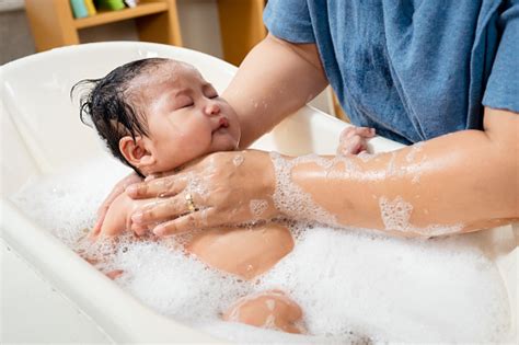 싱글맘의 아시아 손이 손을 뻗어 갓 태어난 딸을 목욕시키기 위해 소녀의 몸보다 큰 욕조 비누 거품으로 가득 찬 소녀의 머리와 몸을 포함한 욕조에서 목욕을했습니다 목욕하기에