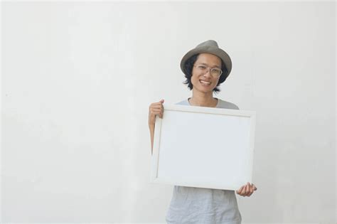 화이트 보드를 들고 카메라에서 웃는 안경 및 모자를 가진 젊은 아시아 남자의 초상화 가방에 대한 스톡 사진 및 기타 이미지