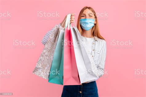 그녀의 얼굴에 의료 마스크를 착용 행복 한 소녀 쇼핑 백으로 포즈를 취하고 분홍색 배경에 카메라를 보고 쇼핑 코로나바이러스 검역