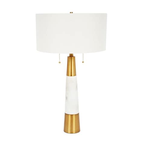 A White And Gold Table Lamp With A White Shade On The Top Standing Against A White Background